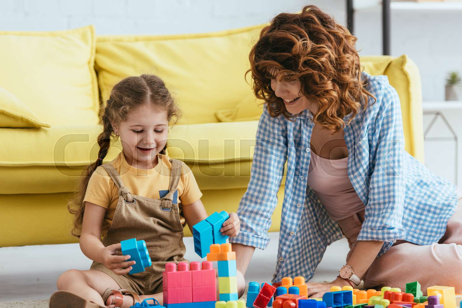 cheerful babysitter and child playing with building blocks while ...