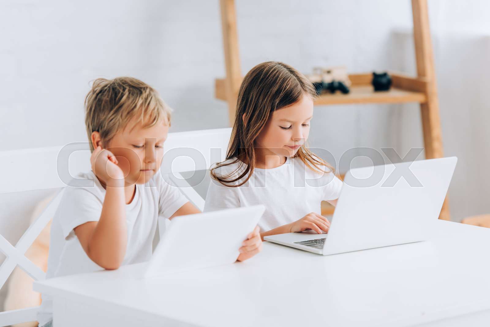 concentrated brother and sister sitting at while table and using ...