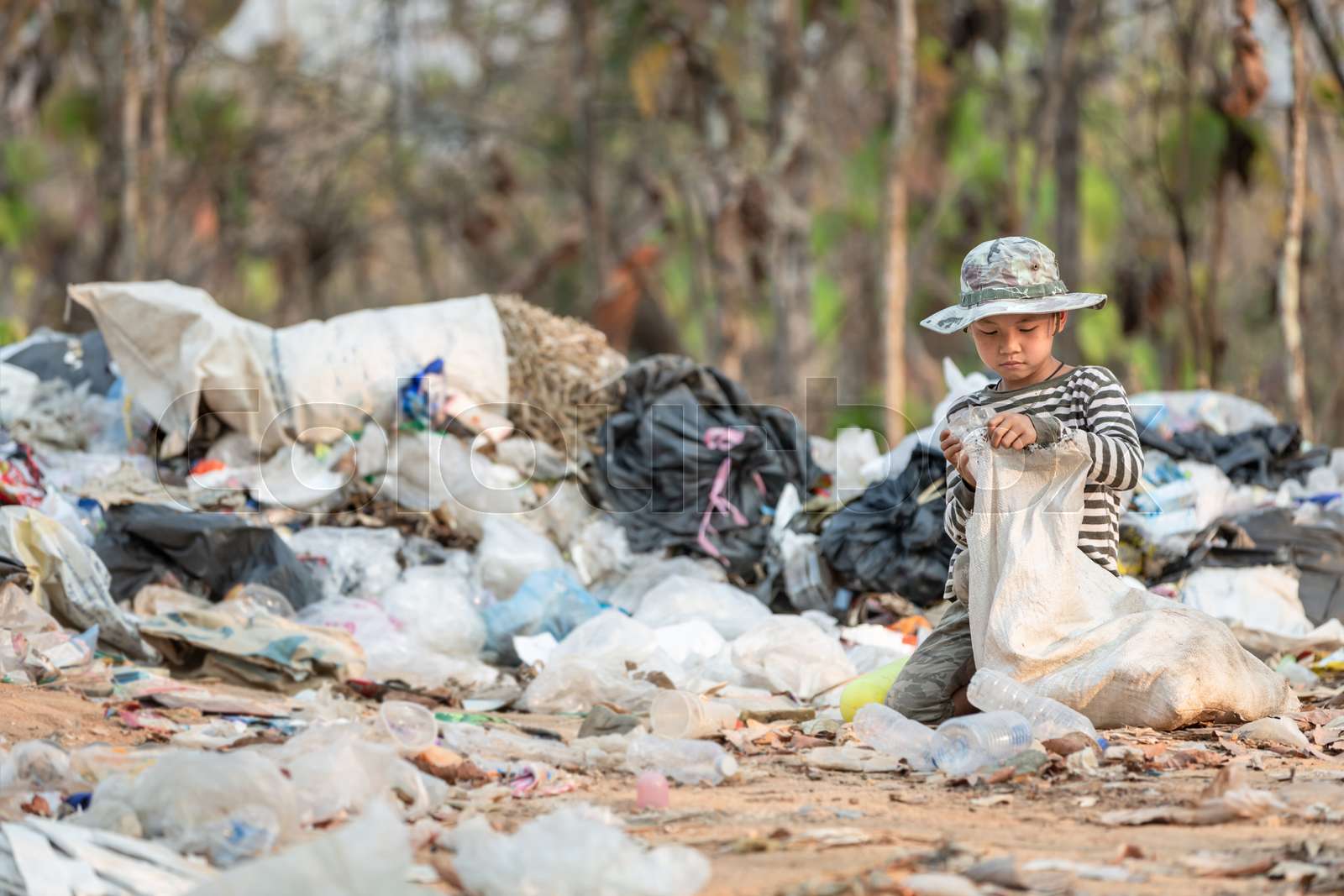 A poor boy collecting garbage waste from a landfill site. Concept of ...
