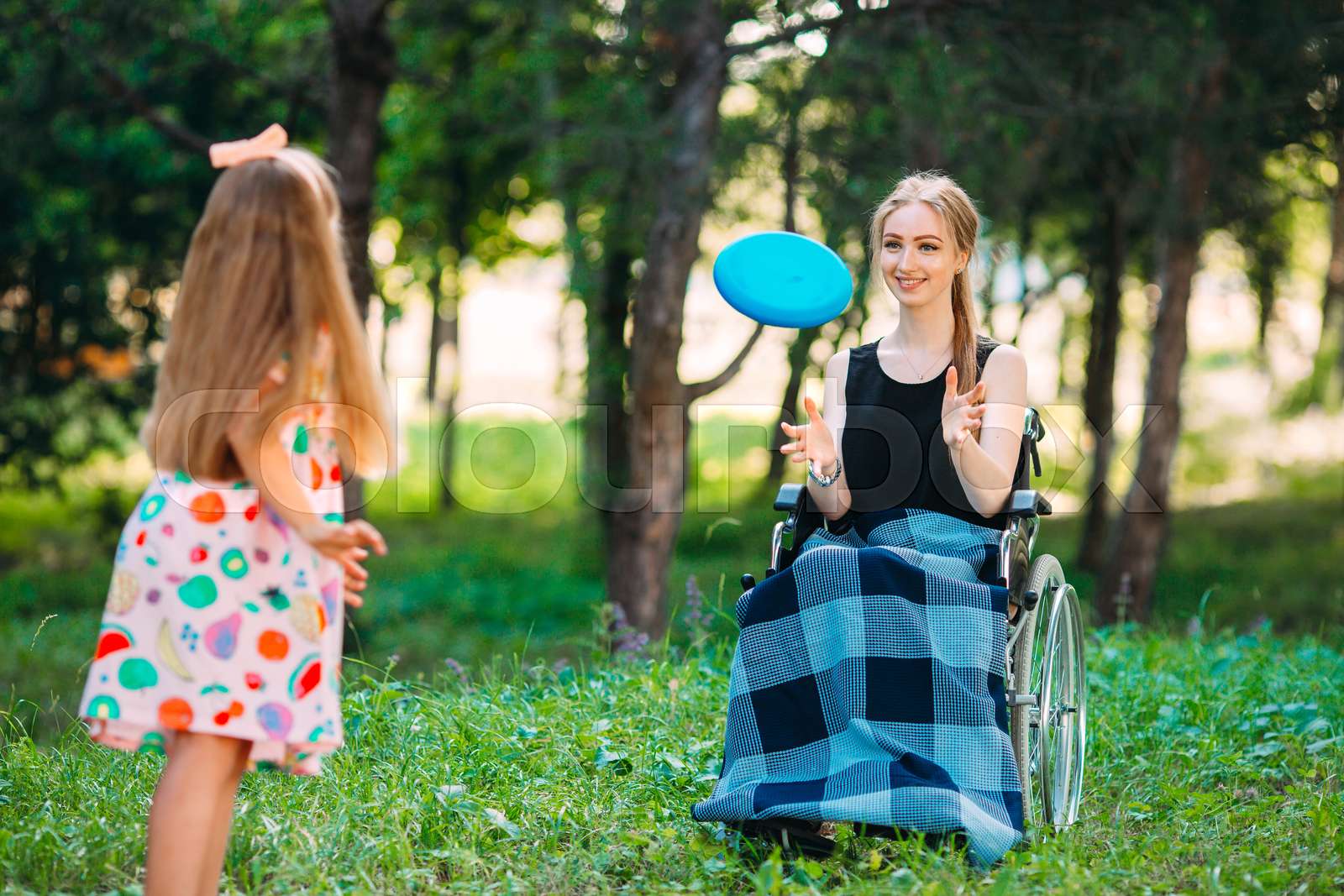 A young disabled girl plays Frisbee with her younger sister ...