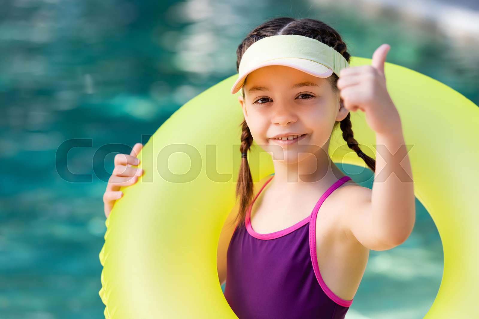 girl in swimsuit and sun visor cap showing thumb up while holding inflatable ring | Stock image ...