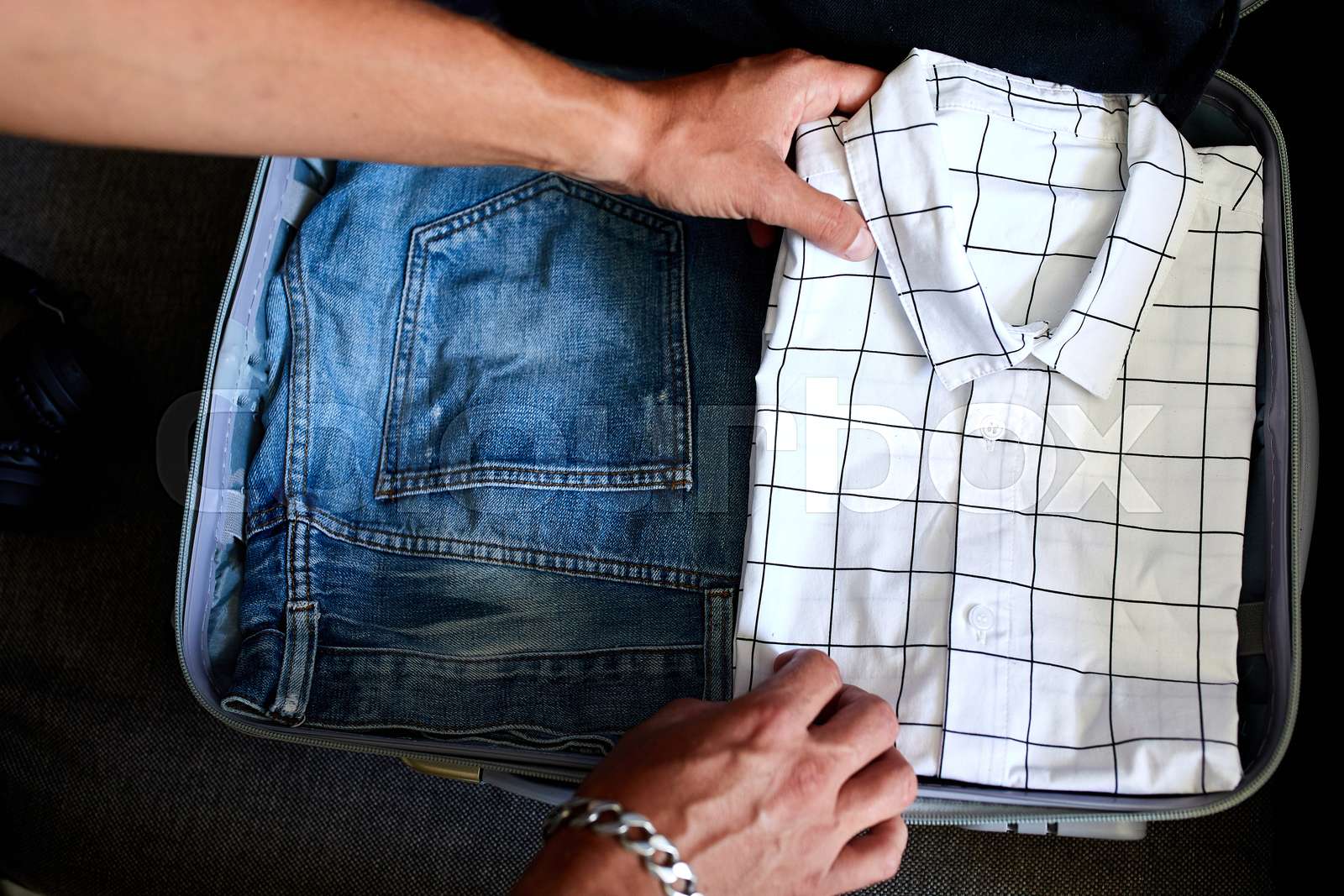 Hands of unrecognisable man packing his casual jeans, shirts in ...