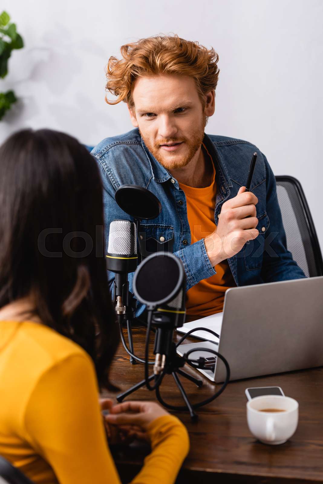 back view of brunette woman near young redhead interviewer in radio ...