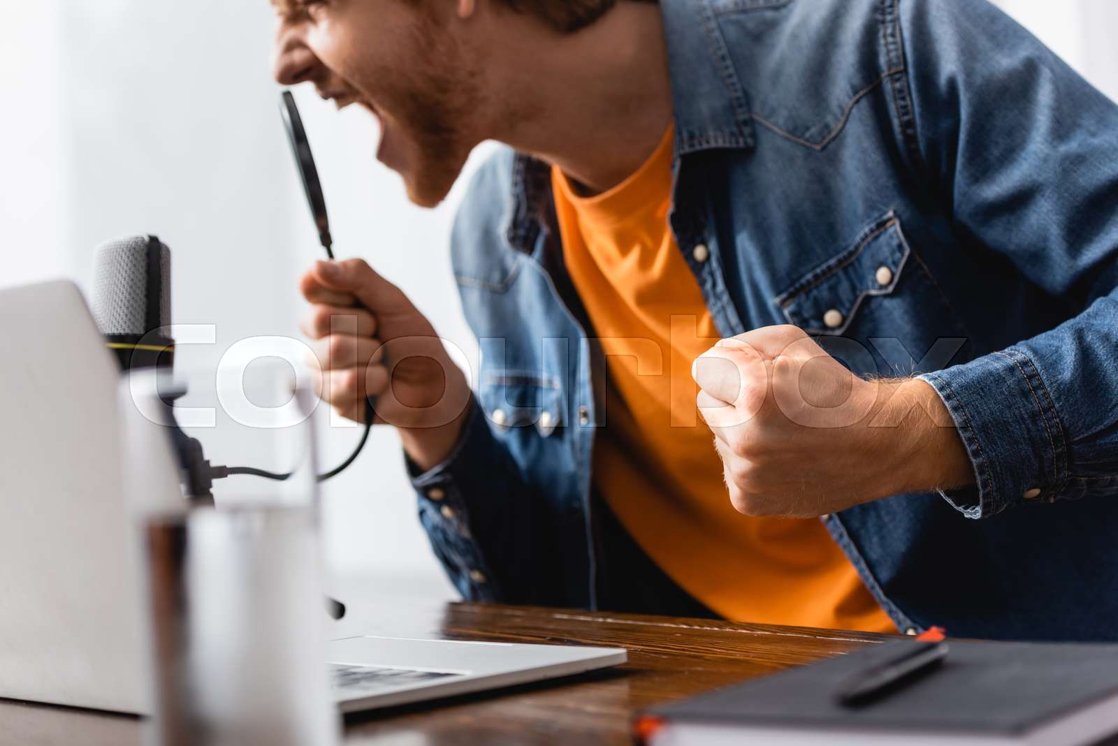 selective focus of angry broadcaster with clenched fist screaming in ...