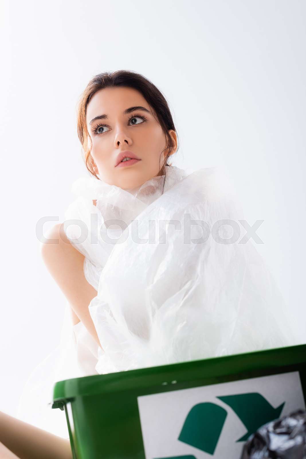 brunette woman wrapped in plastic bag sitting near trash bin with ...