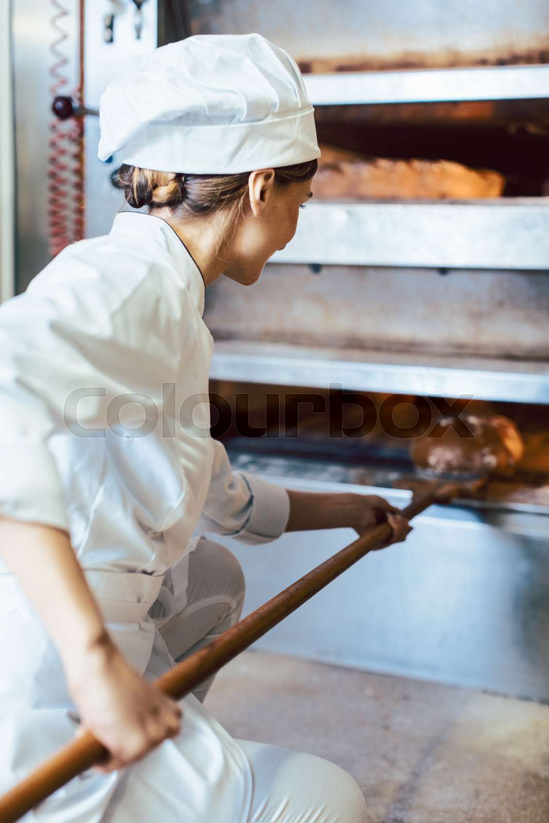 Baker putting bread in the bakery oven | Stock image | Colourbox