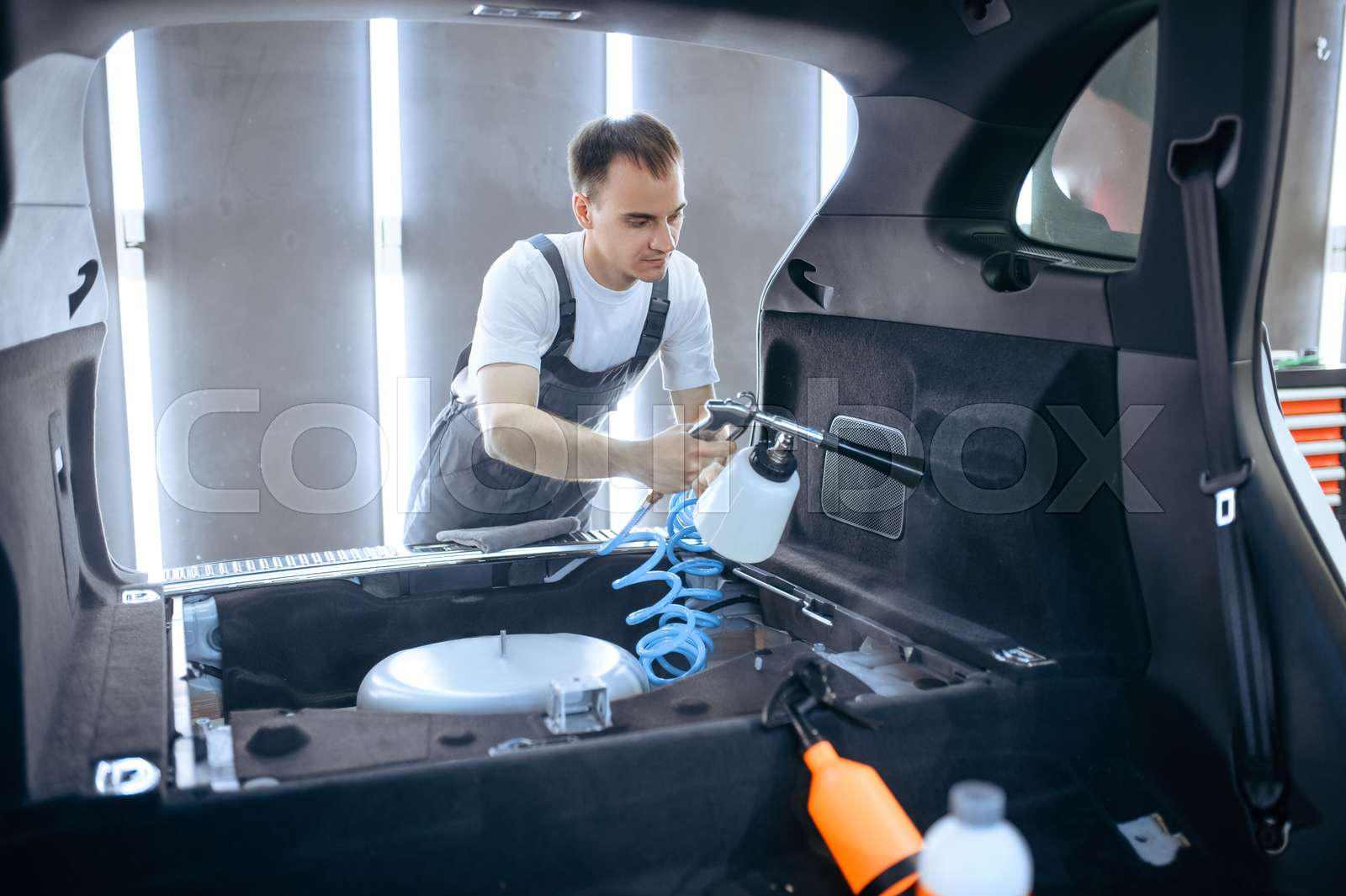 Worker sprays car trunk, dry cleaning, detailing | Stock image | Colourbox