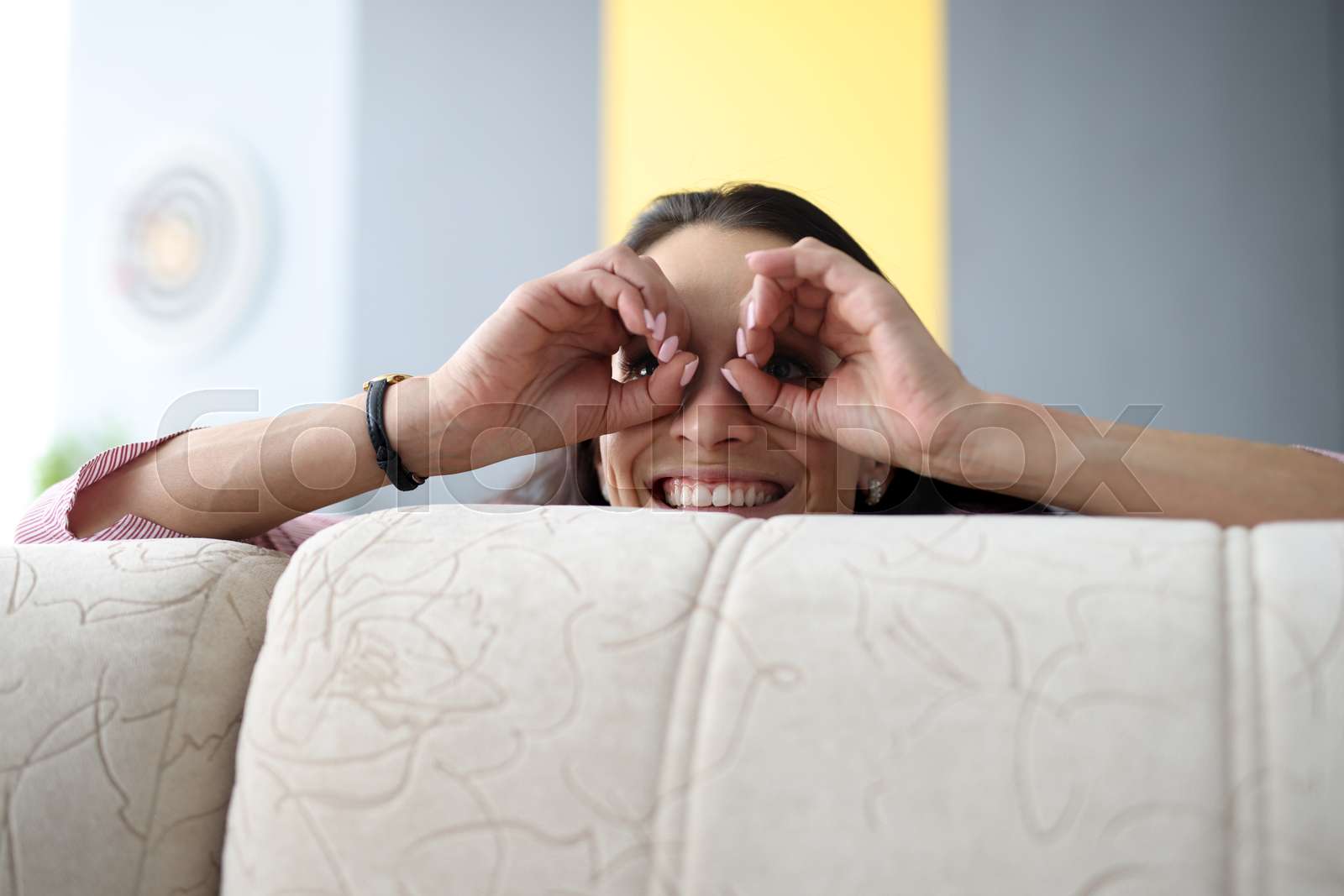 Cheerful woman peek from behind sofa. | Stock image | Colourbox