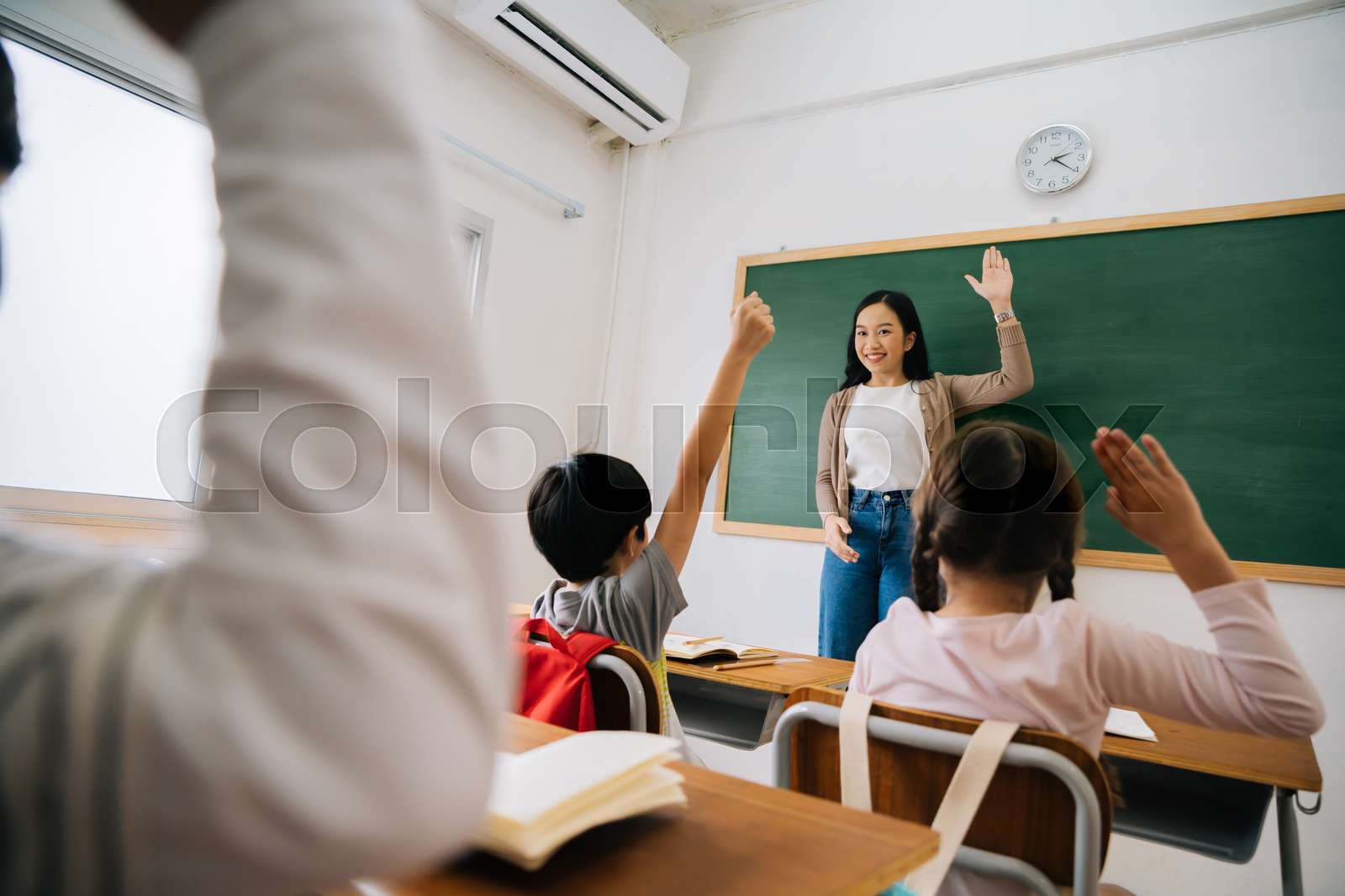 Asian school teacher with students raising hands. Young woman working ...