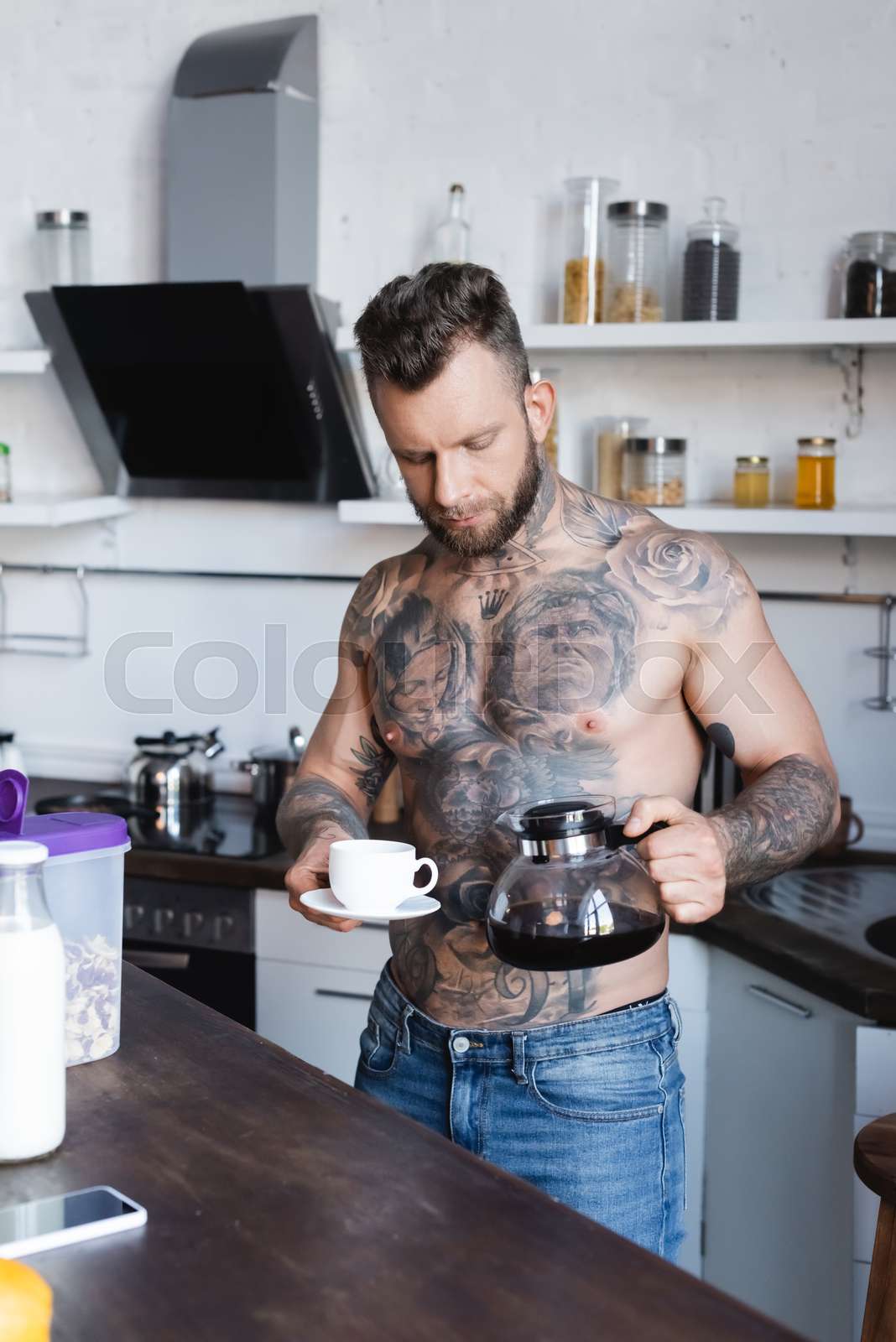 shirtless, tattooed man holding coffee pot and cup in kitchen | Stock ...