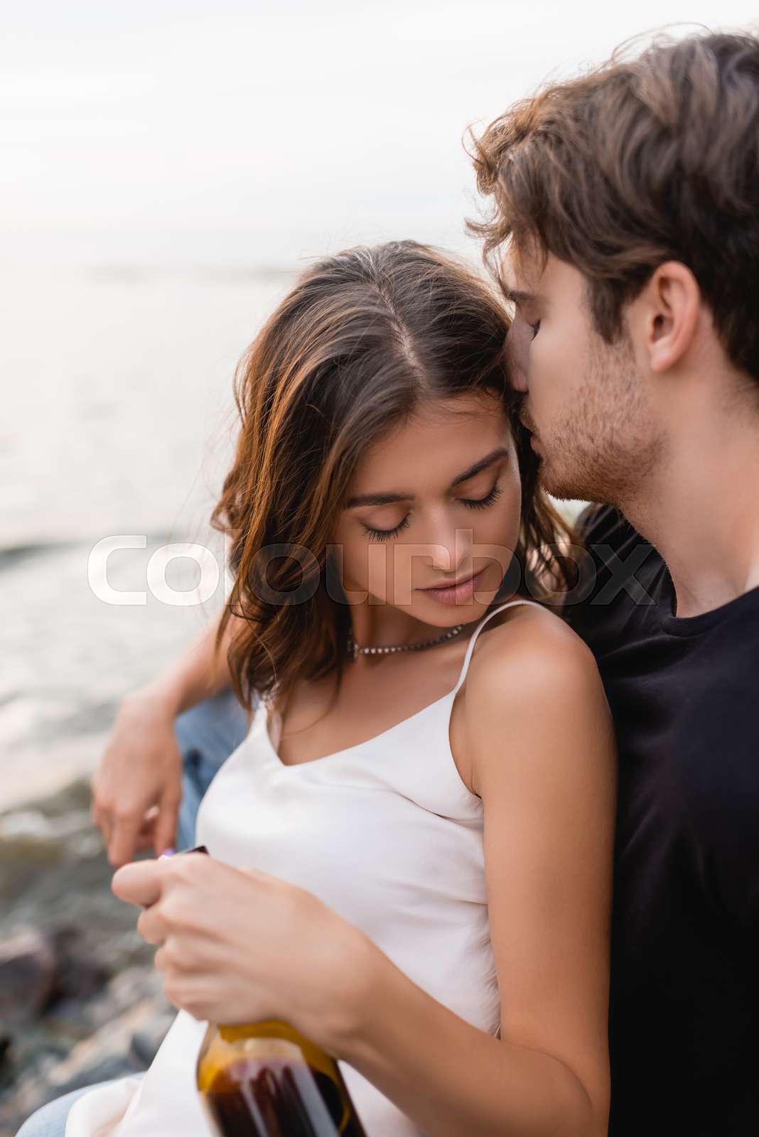 Selective Focus Of Young Man Kissing Girlfriend With Bottle Of Wine On Beach Stock Image