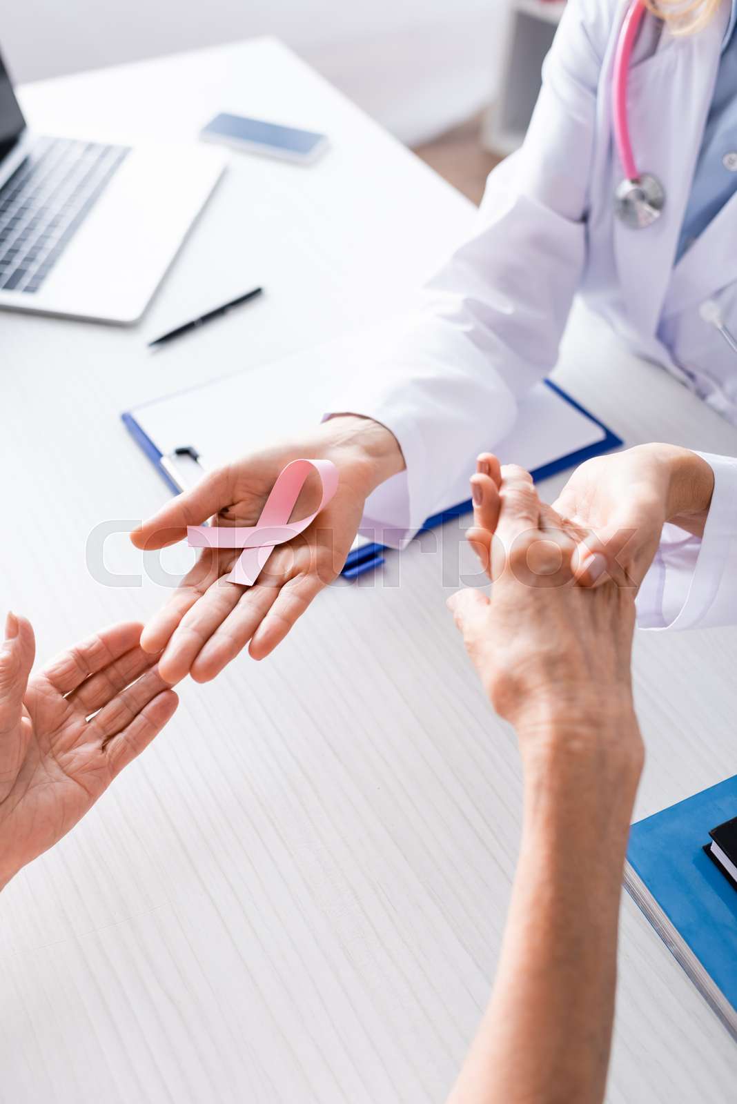 Cropped view of doctor holding patient hands and showing pink ribbon ...