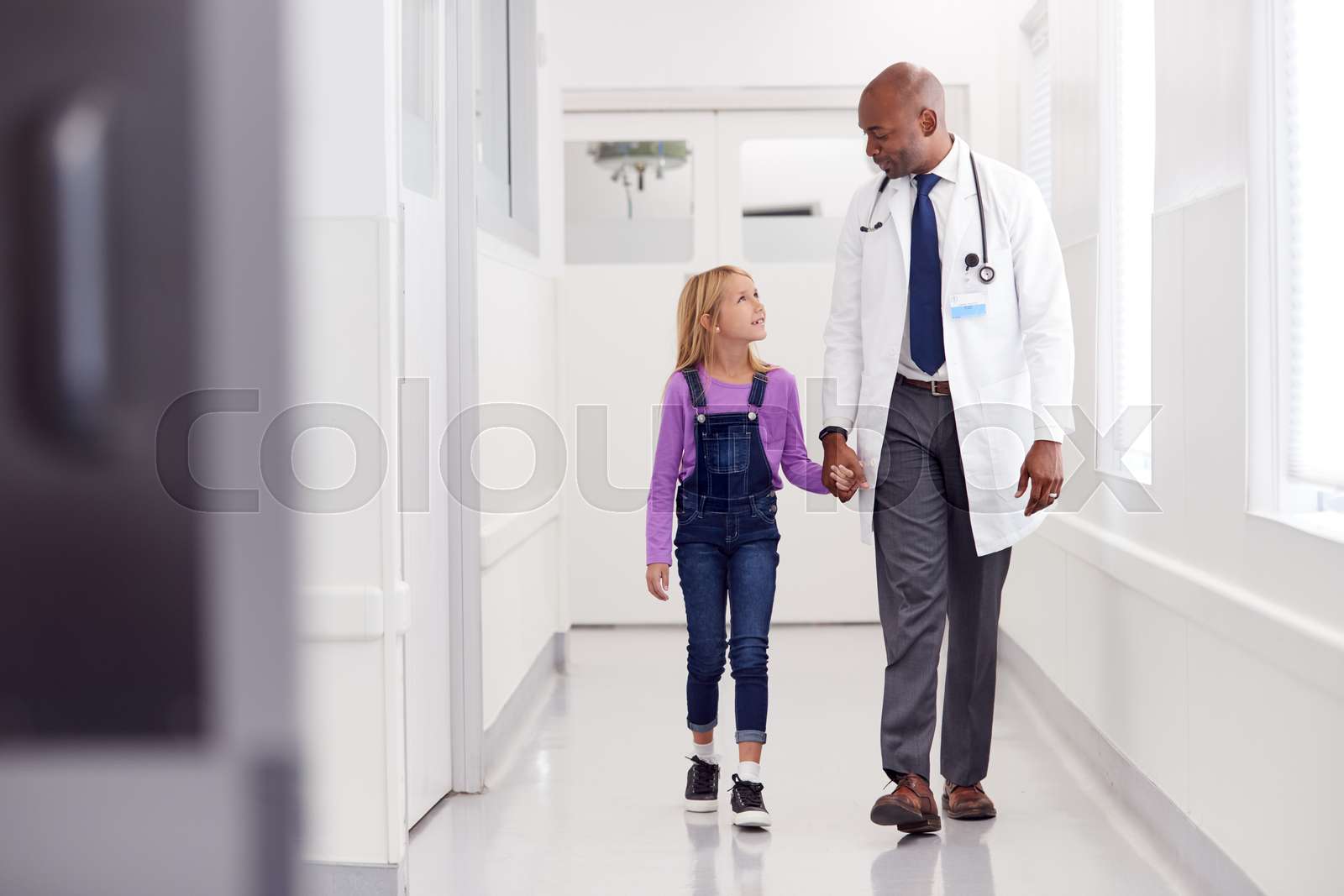 Male Paediatric Doctor Walking Along Hospital Corridor Holding Hands ...