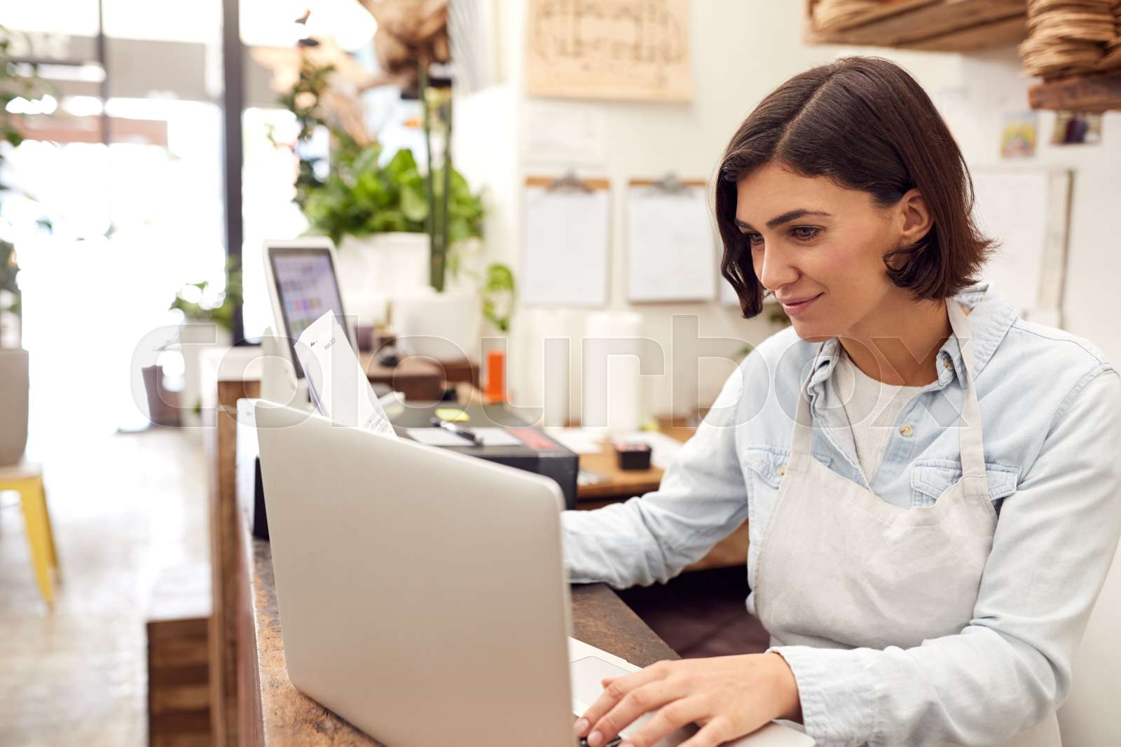 Female Sales Assistant Working On Laptop Behind Sales Desk Of Florists ...