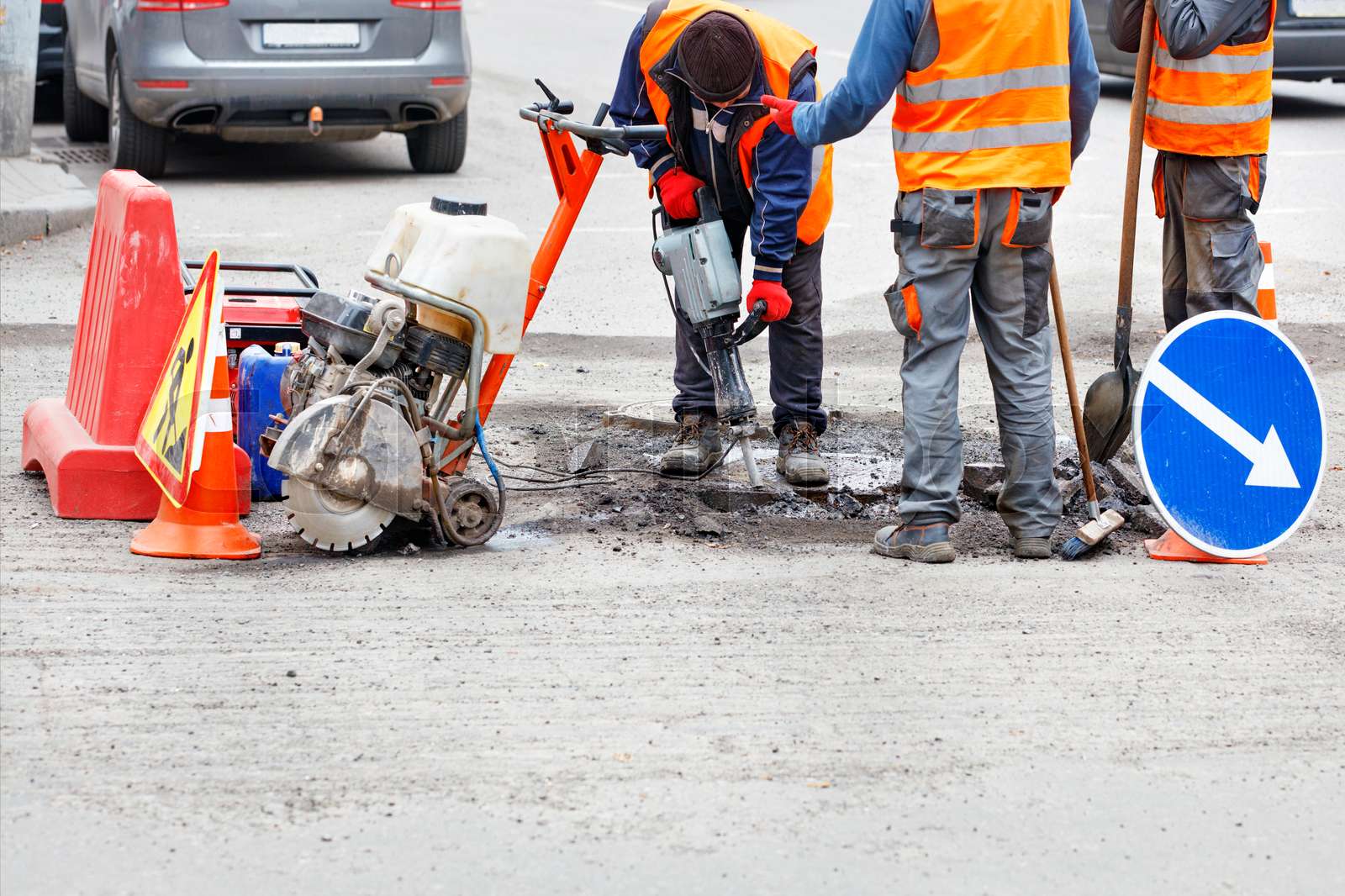 A team of road workers with hand-held road tools are repairing a ...