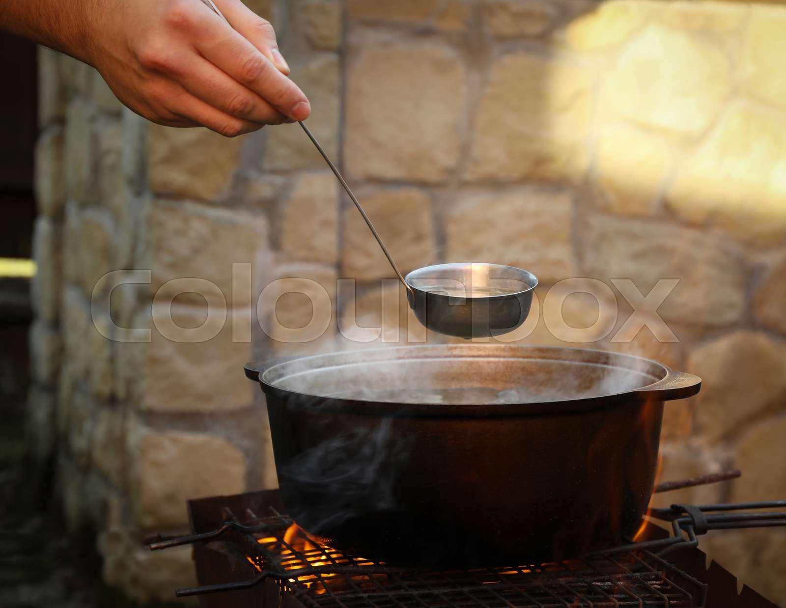 Man holding ladle over metal cauldron with soup on fire | Stock image ...