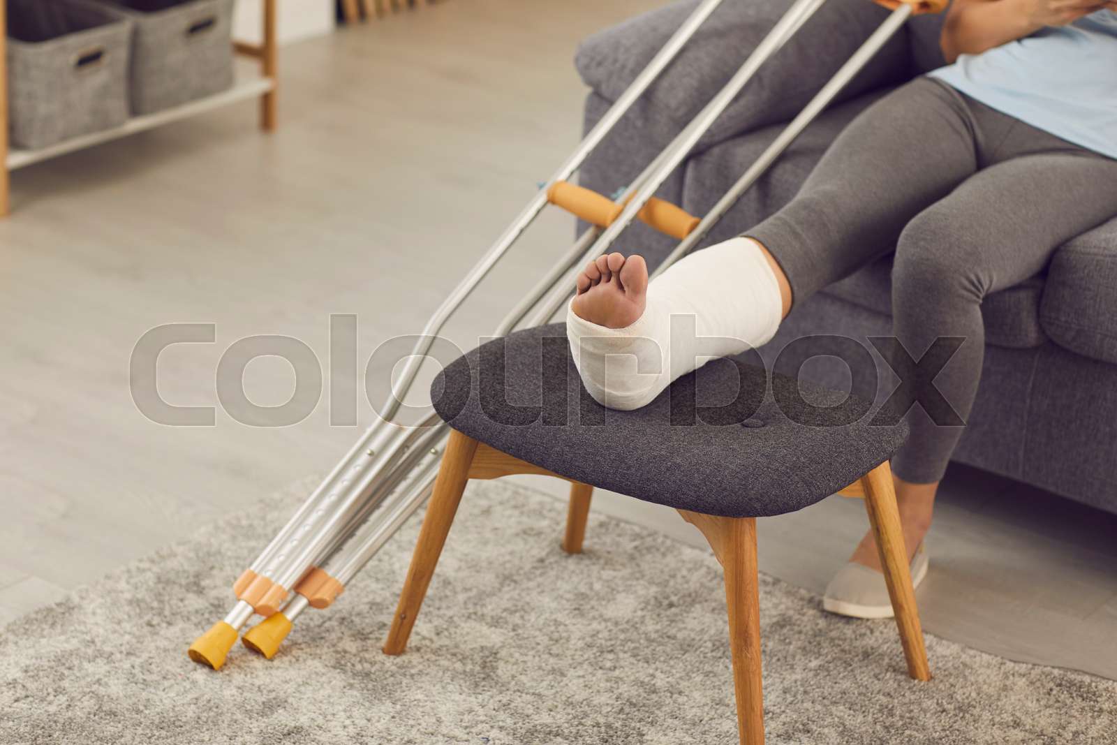 Close-up of females broken leg on stool in cast and metal crutches ...