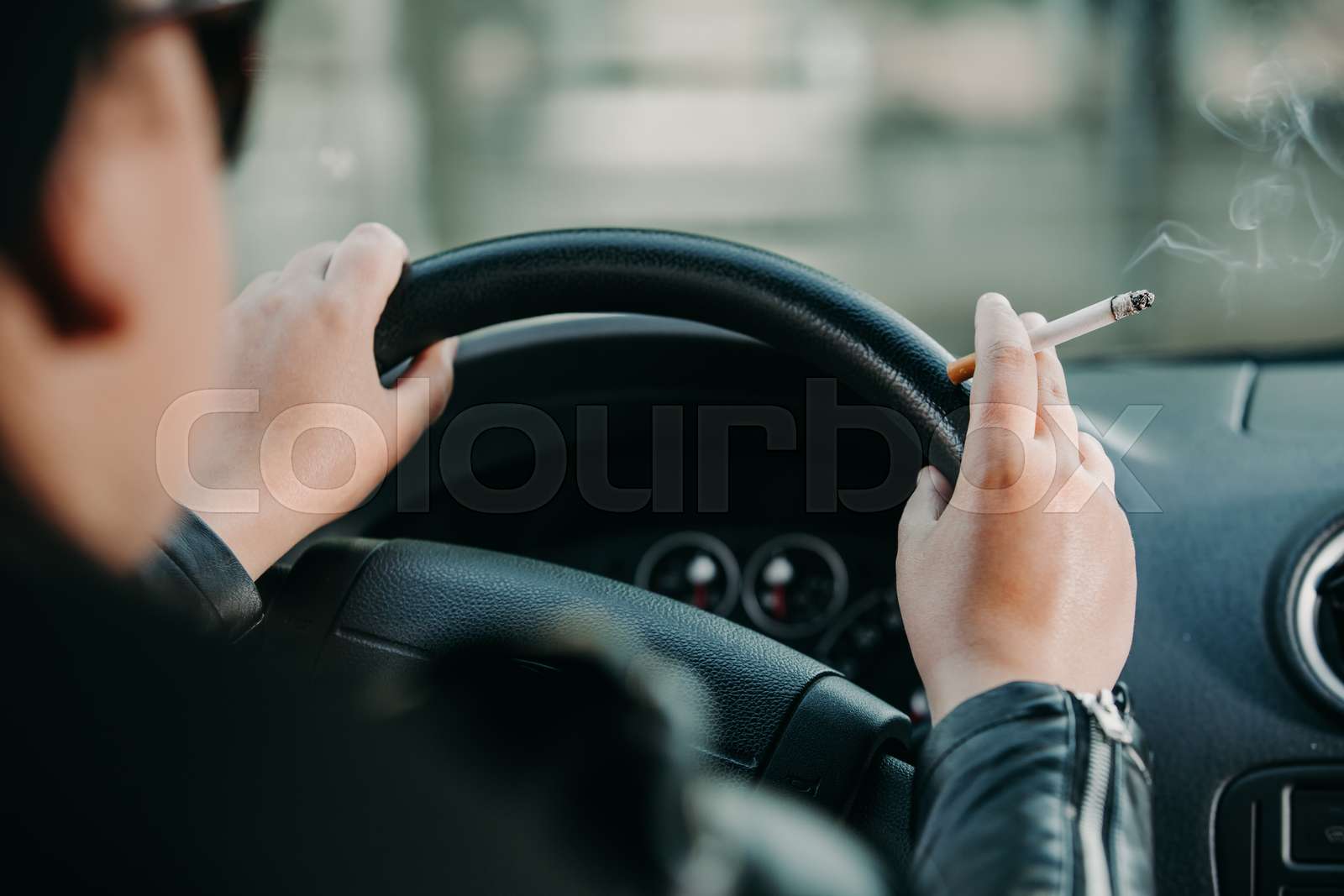Young woman smoking a cigarette while driving a car, transportation ...