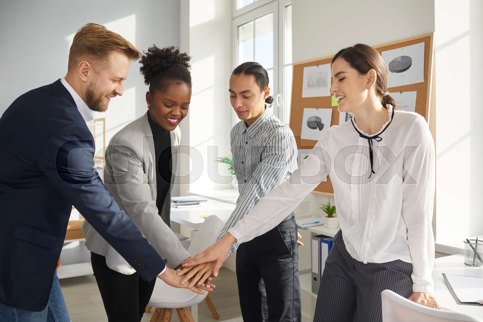 Multiracial colleagues fold their hands on each other as a symbol of ...