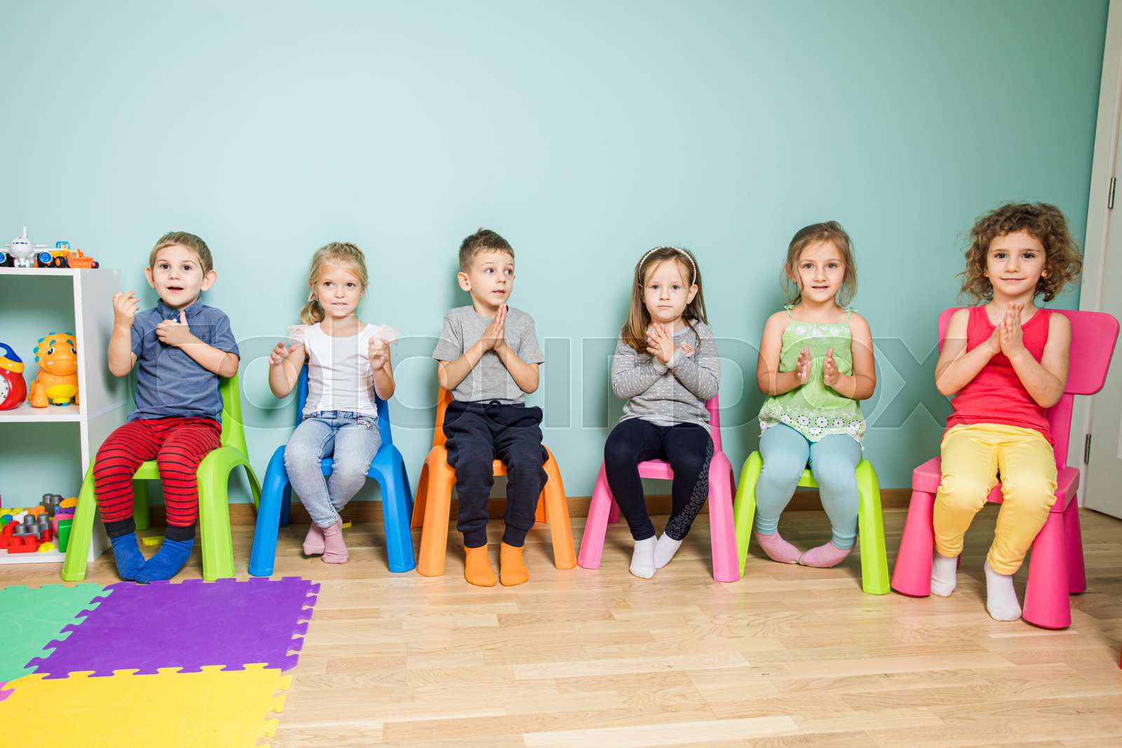 Kids are sitting on the colorful chairs, clapping hand | Stock image ...