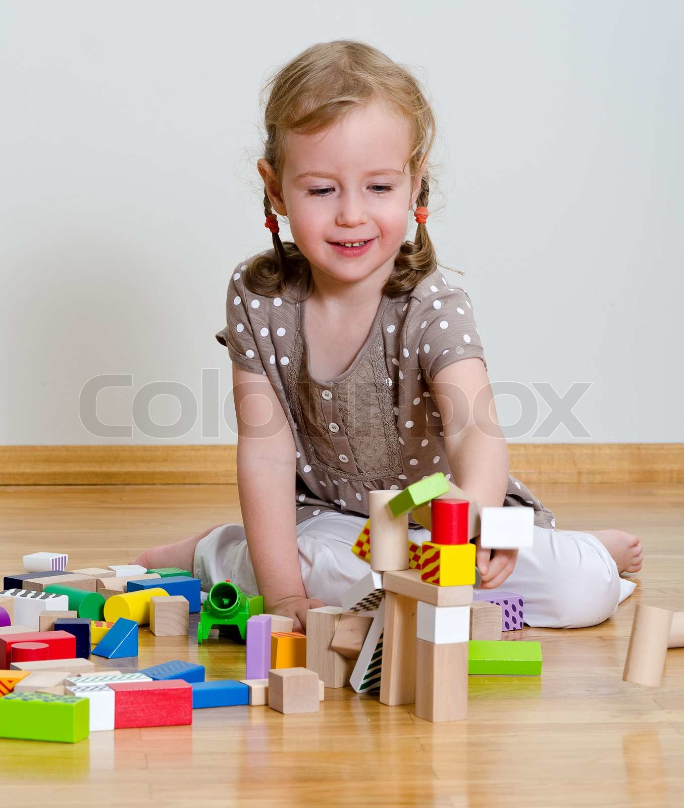 Cute little girl sitting on the floor and playing with building blocks ...