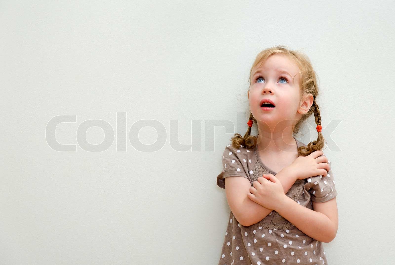 Portrait of little girl standing against the wall and looking up ...