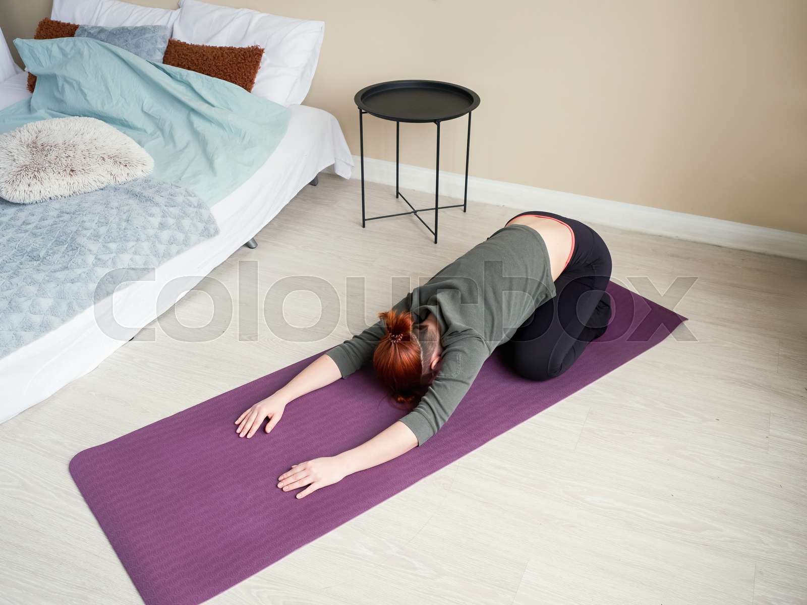 Woman doing asanas on yoga mat near bed. Stretching exercises in ...