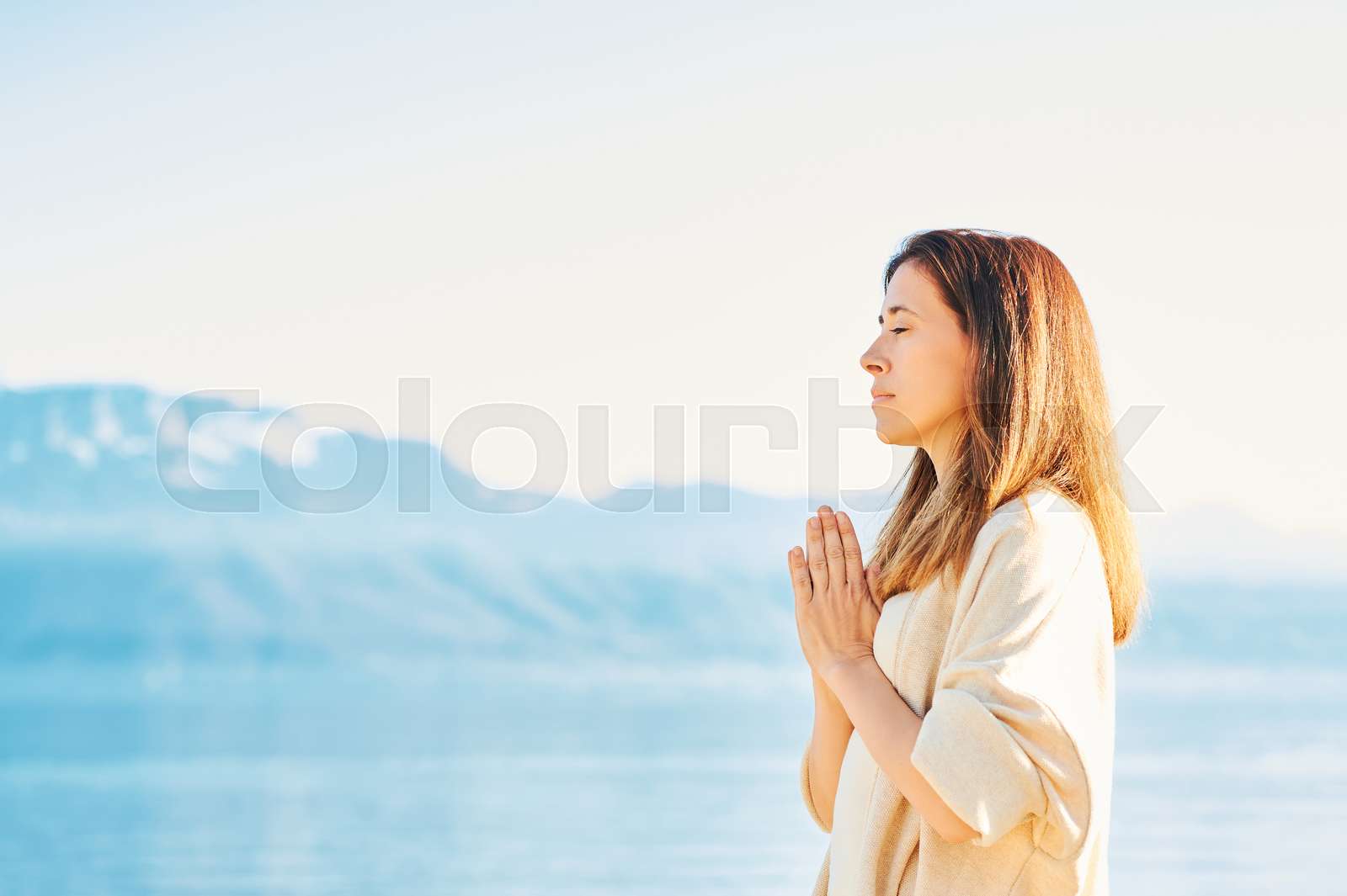 Beautiful spiritual woman meditating by the lake, wearing beige clothes ...
