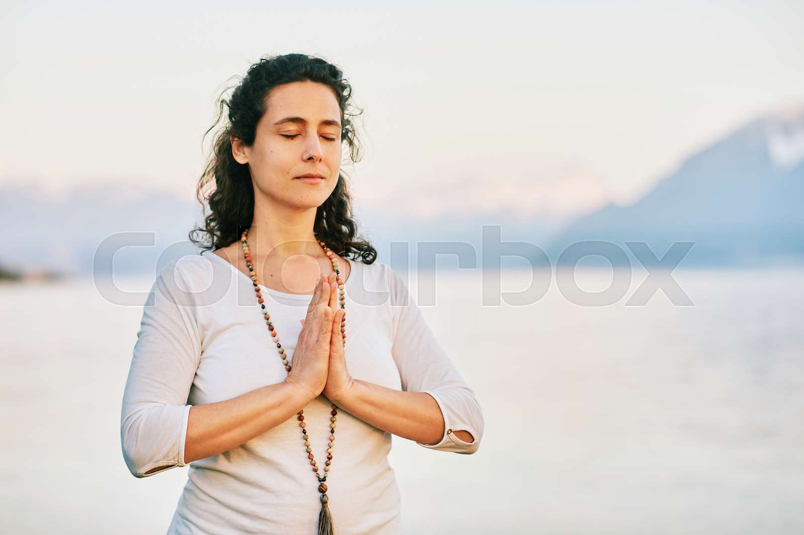 Beautiful spiritual woman meditating by the lake, wearing white clothes ...