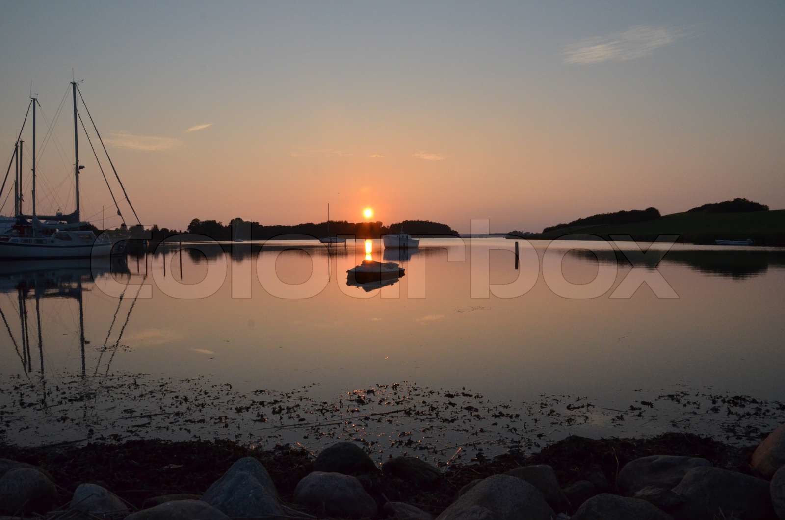 Solnedgang over havet med med sol og land i horisont i orange og sorte ...