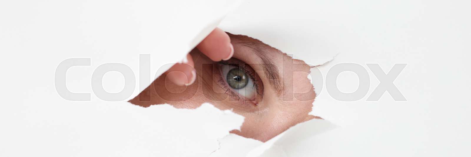 Female eye looks through hole in white paper | Stock image | Colourbox