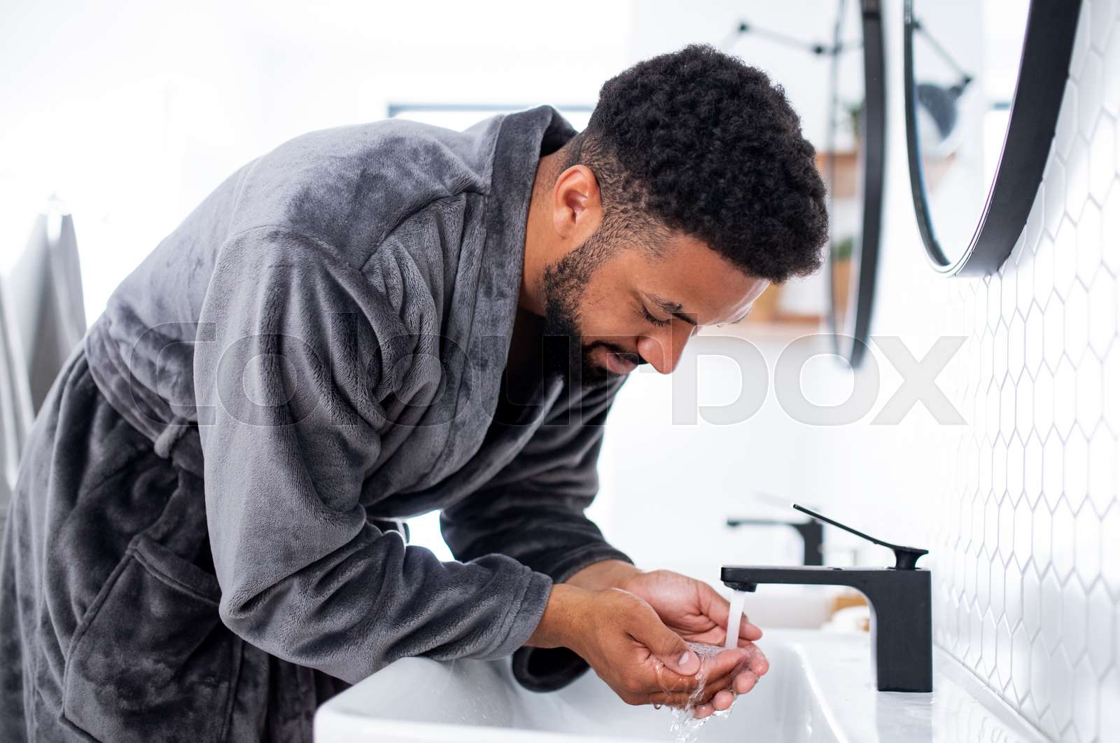 Young man washing face indoors at home, morning or evening routine ...