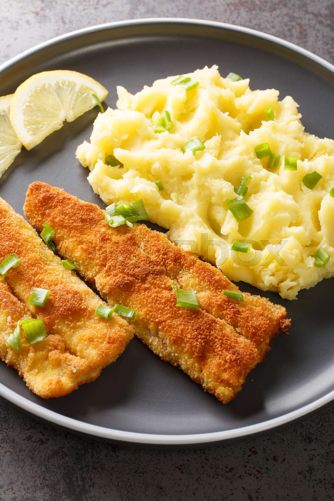 Breaded fried fish and mashed potatoes and lemon close-up in a plate ...