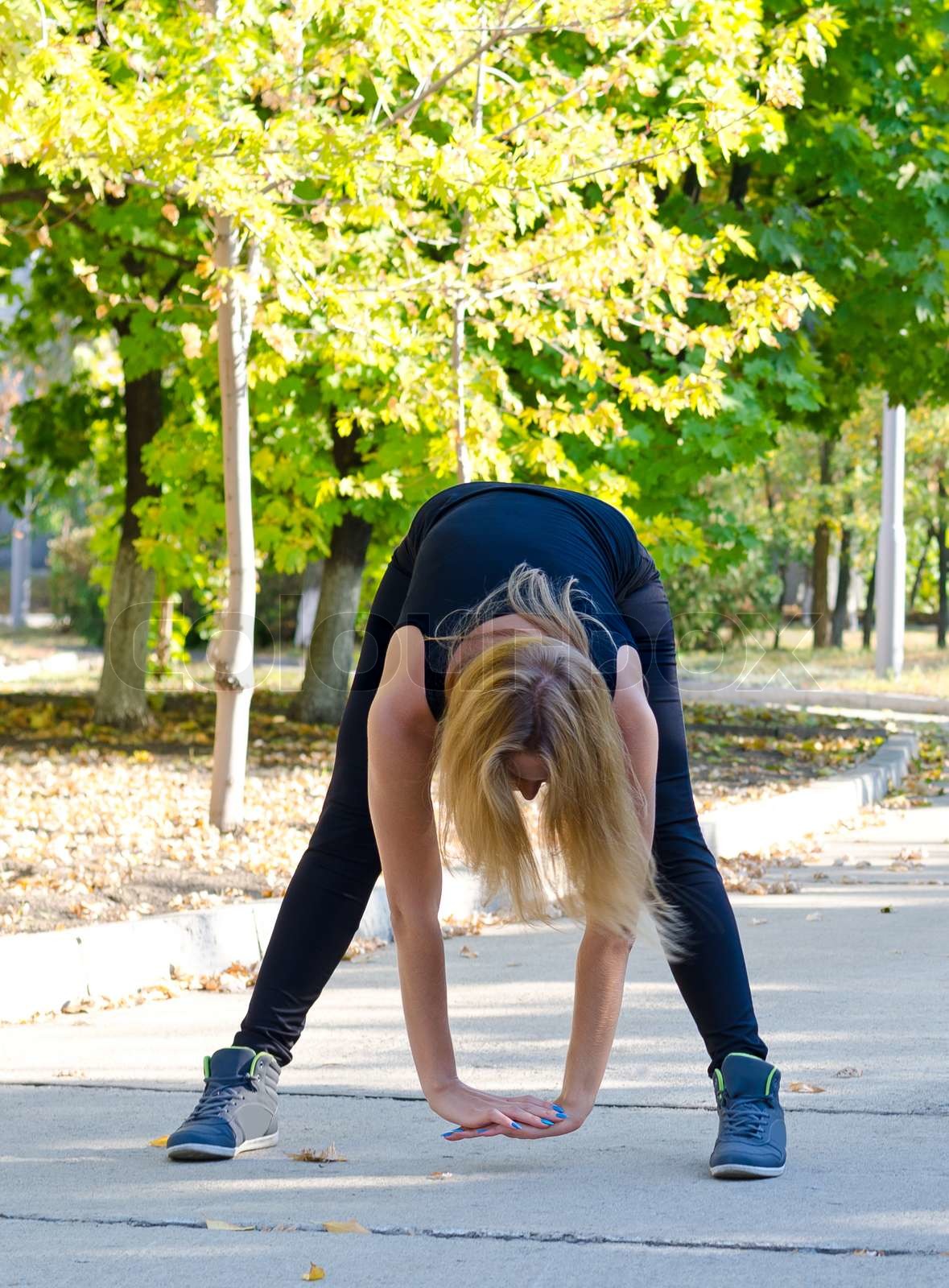 Woman limbering up for exercises bending down towards the ground with ...