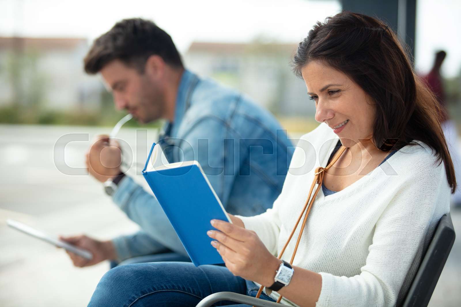 woman reading a book and man looking at tablet outdoors | Stock image ...