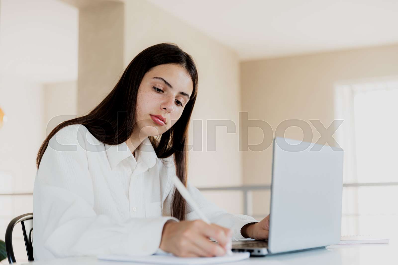 Woman sitting at desk, reading from laptop, writing notes at her ...