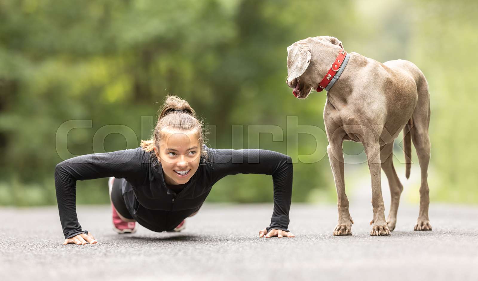 Young woman doing pushups outdoors smiles at her dog observing her ...