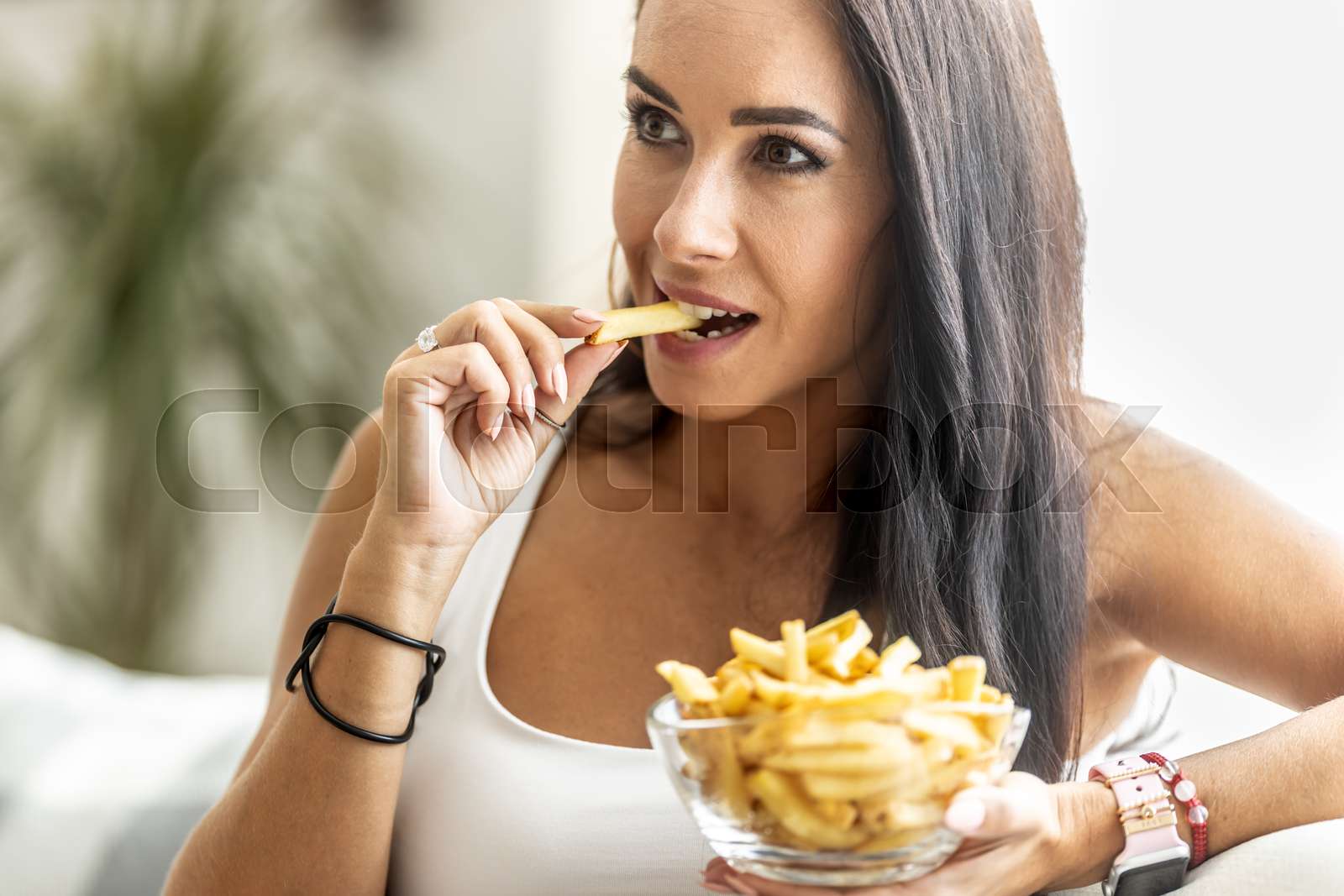 Woman eating a bowl of chips bites into crispy yellow french fried in ... Woman eating a bowl of chips bites into crispy yellow french fried in ...