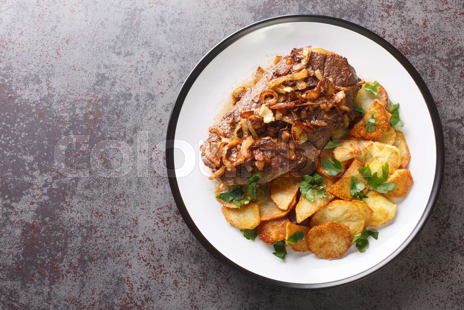 German beef steak Rostbraten with onion and fried potatoes closeup on ...