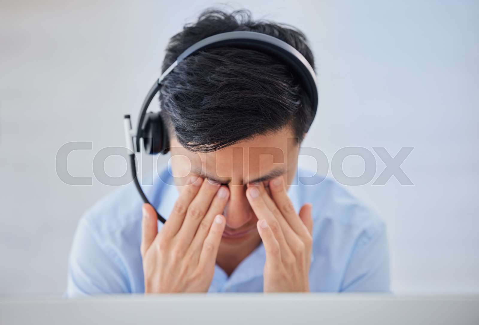 Stressed young asian male call centre agent getting a headache while ...