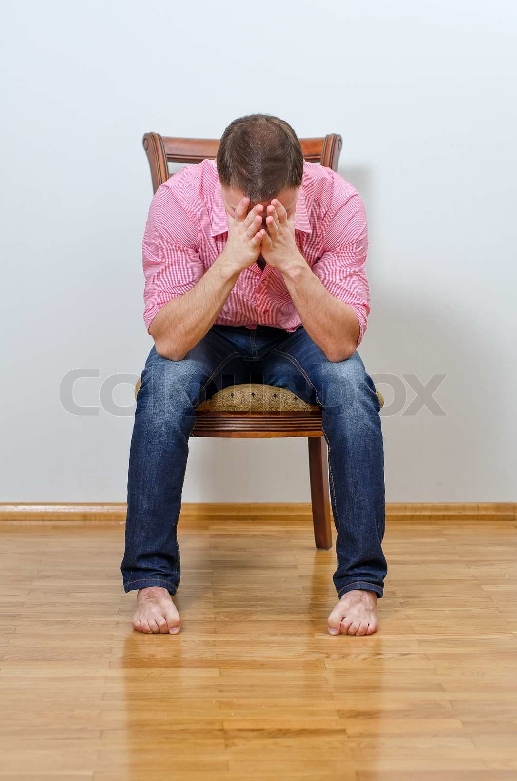 Depressed man sitting on a chair against the wall | Stock image | Colourbox