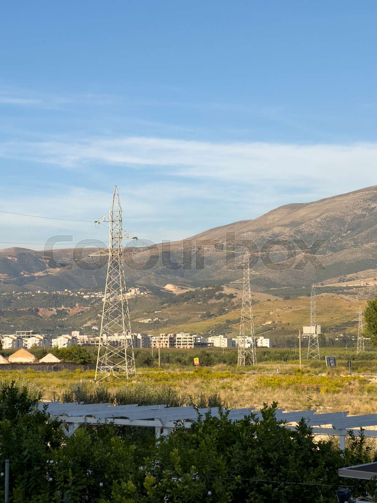Overhead line pylons, high voltage pylons in meadow with mountains on ...