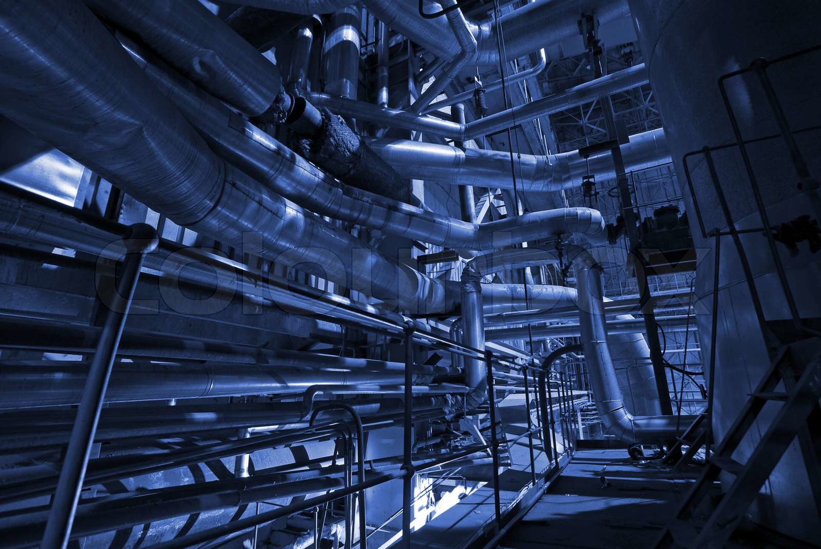 Pipes, tubes, machinery and steam turbine at a power plant in blue tone ...