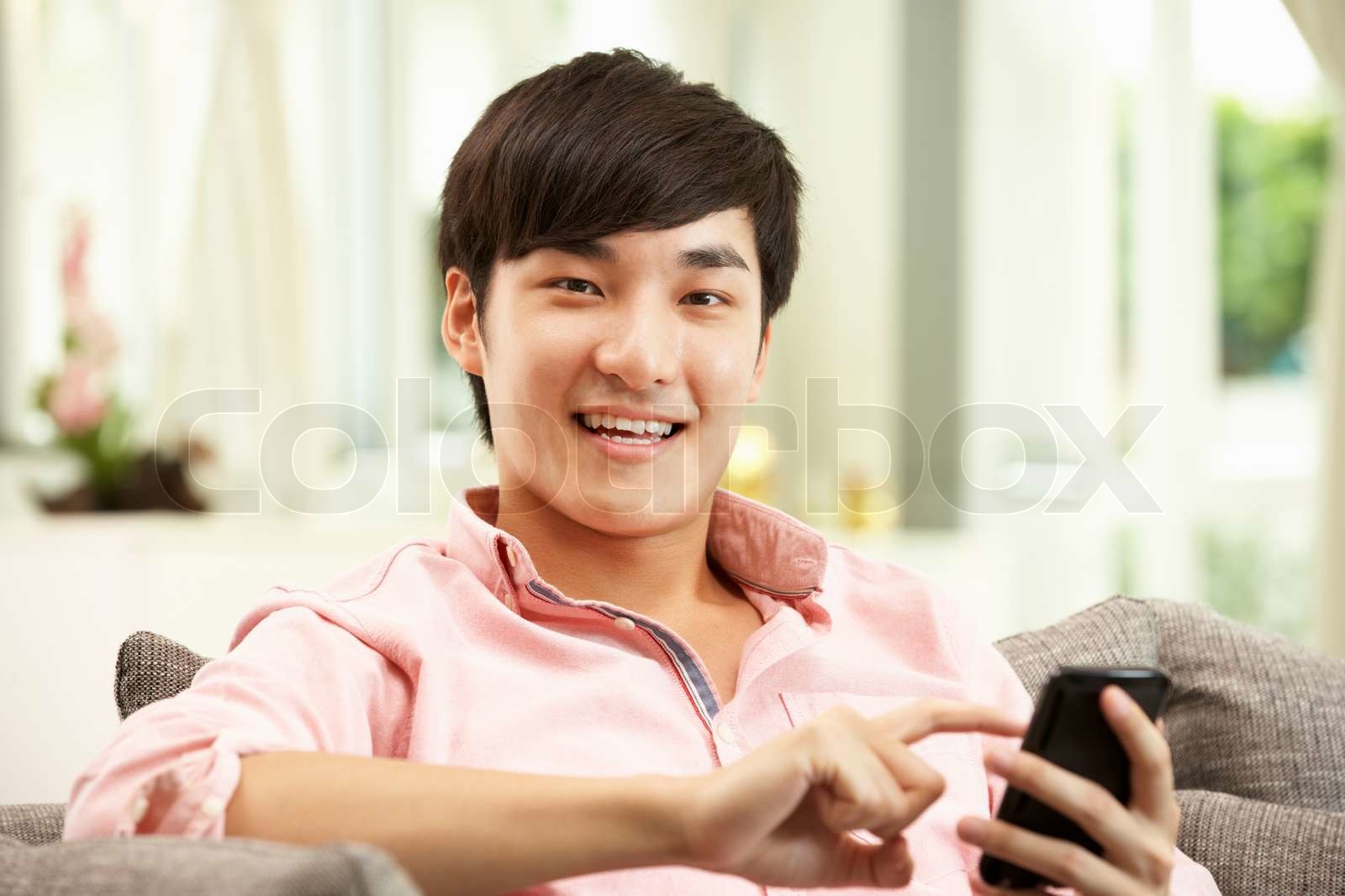 Young Chinese Man Using Mobile Phone On Sofa At Home | Stock image ...