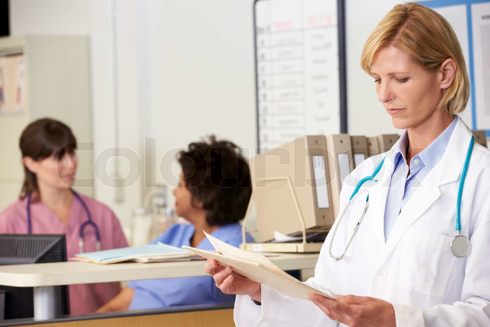 Female Doctor Reading Patient Notes At Nurses Station | Stock image ...