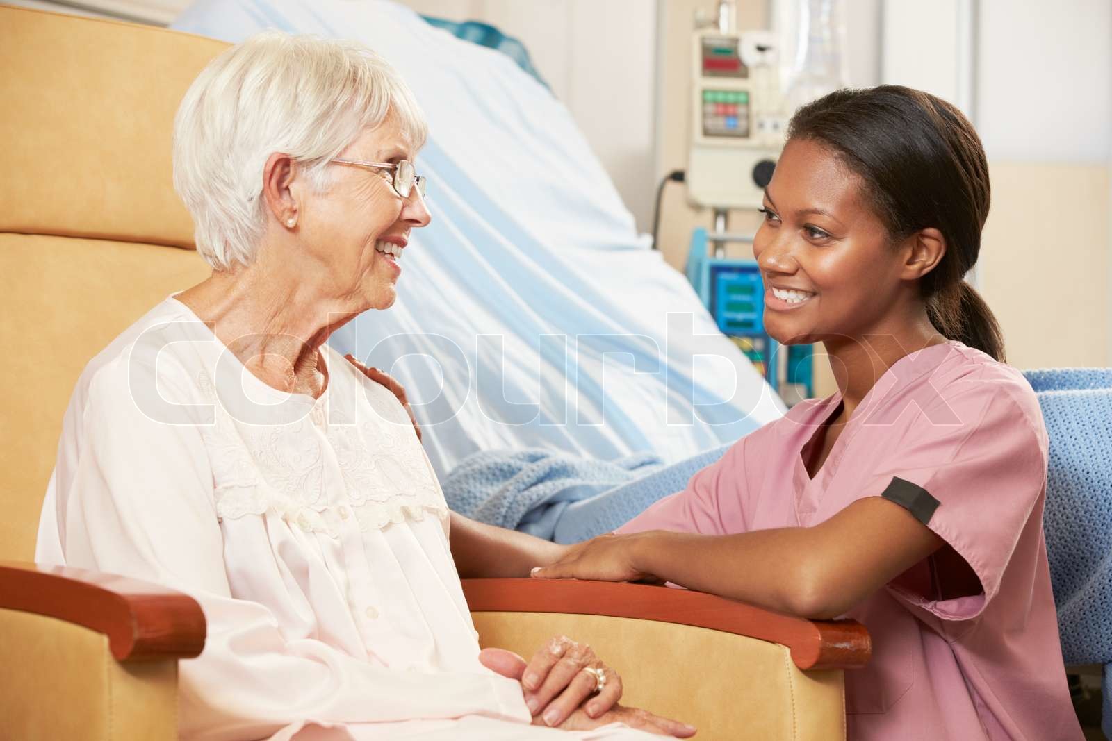 Nurse Talking To Senior Female Patient Seated In Chair By Hospital Bed ...
