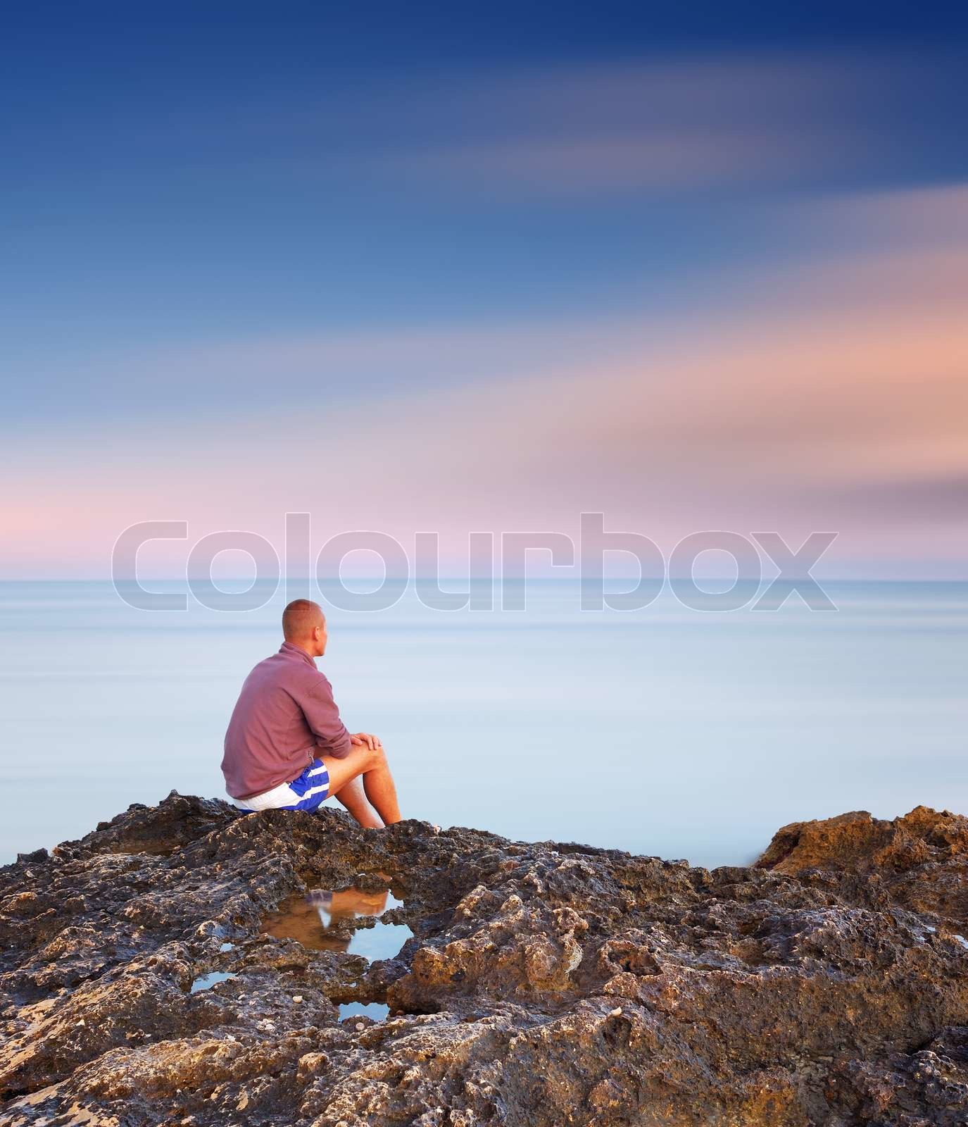 Man sitzt auf einem Felsen am Meer | Stock Bild | Colourbox