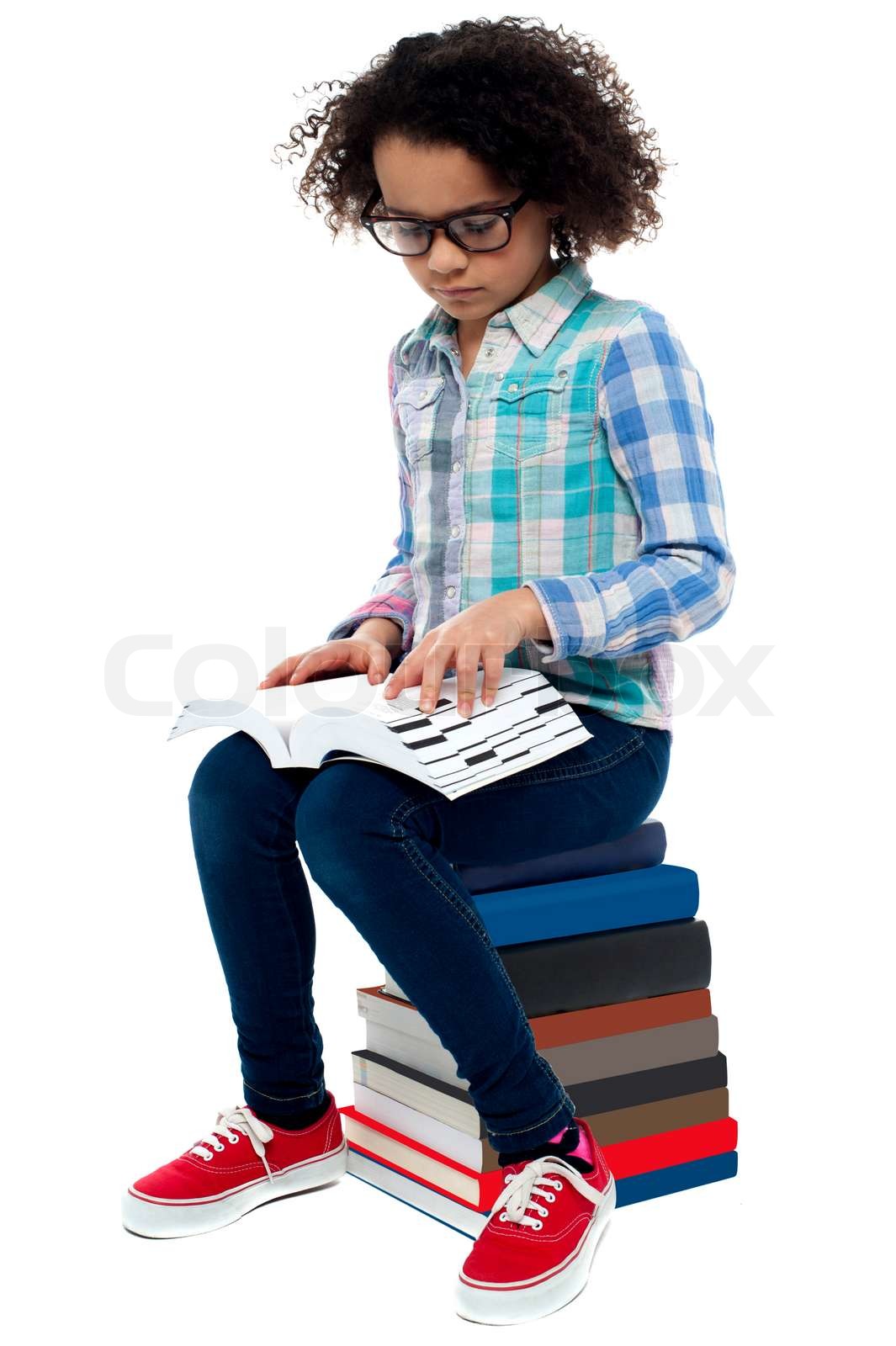 Young kid sitting on stack of books and reading | Stock image | Colourbox