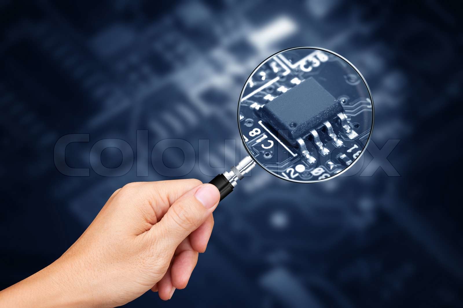 Hand holding magnifying glass with computer chip | Stock image | Colourbox