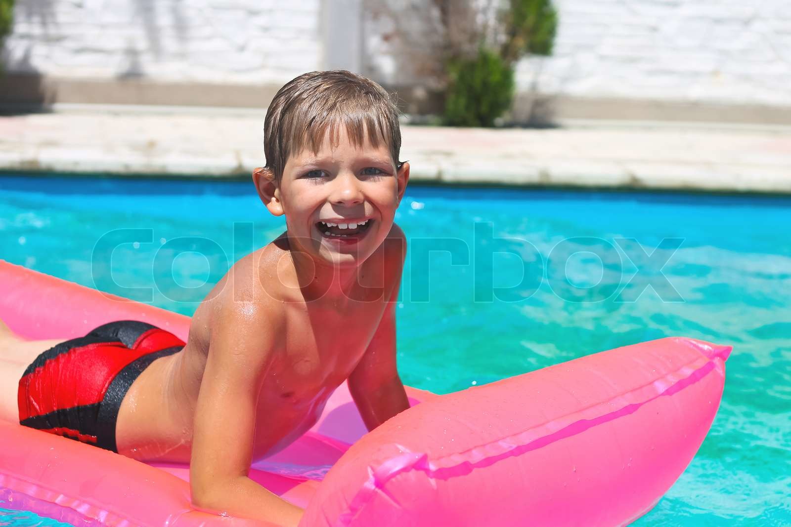 Smiling boy lies on pink mattress in the pool | Stock image | Colourbox